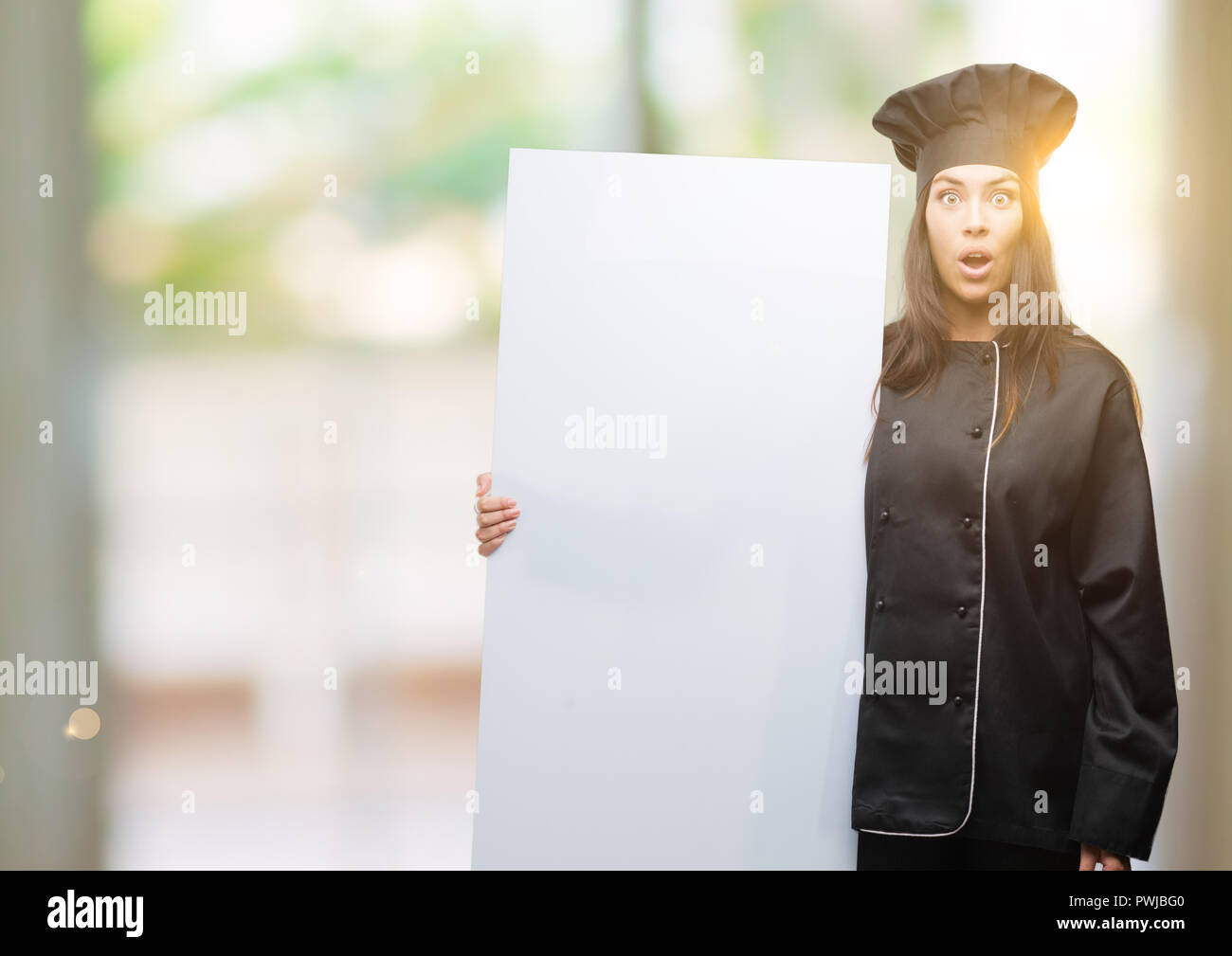 Young hispanic cook woman wearing chef uniform holding banner scared in ...