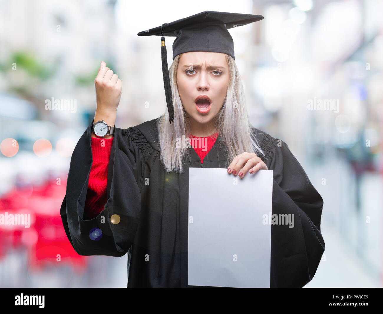 Young blonde woman wearing graduate uniform holding degree over ...