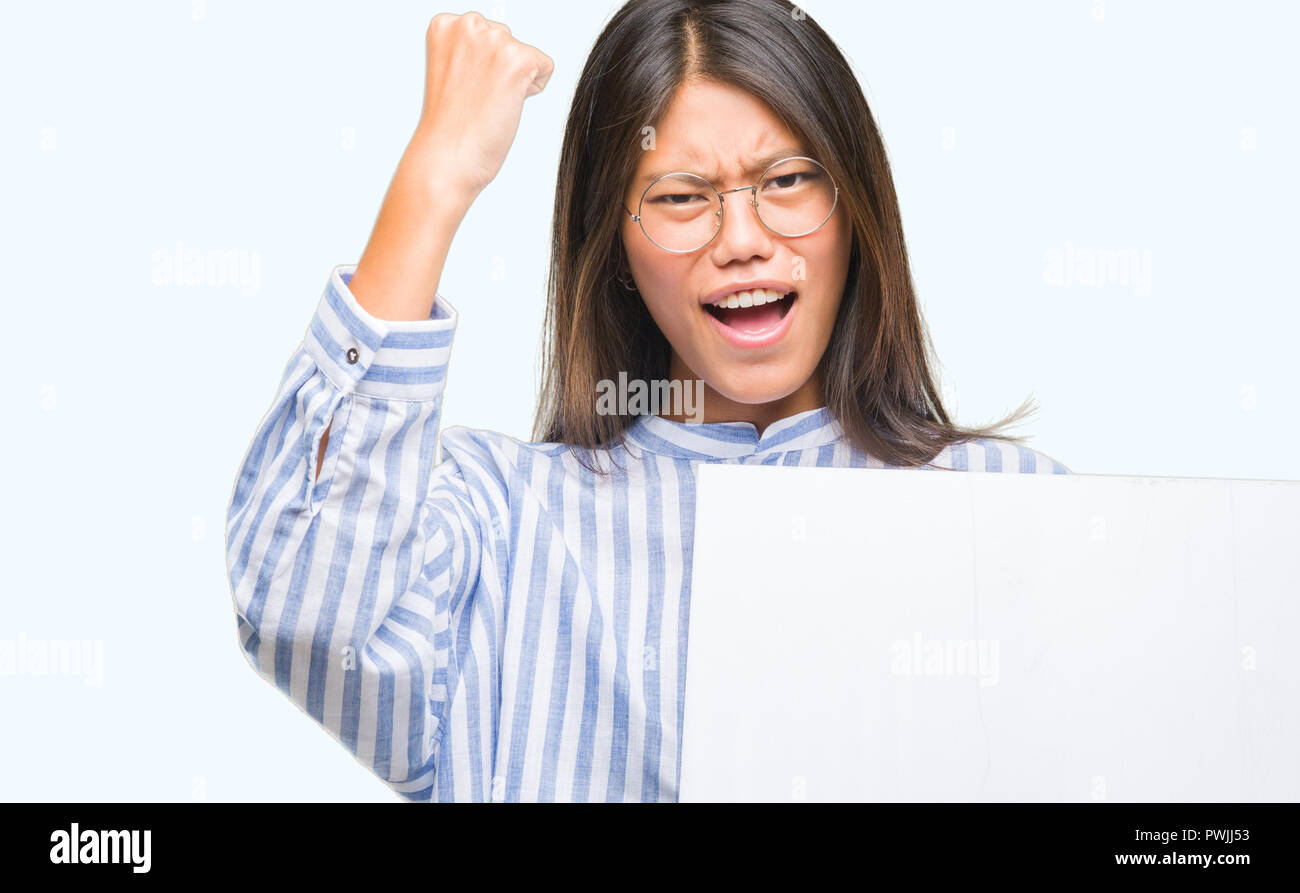 Young asian woman over isolated background holding blank banner annoyed ...
