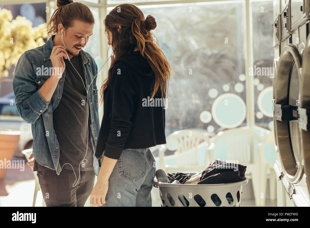 Shy couple standing in the laundry room facing each other listening to ...