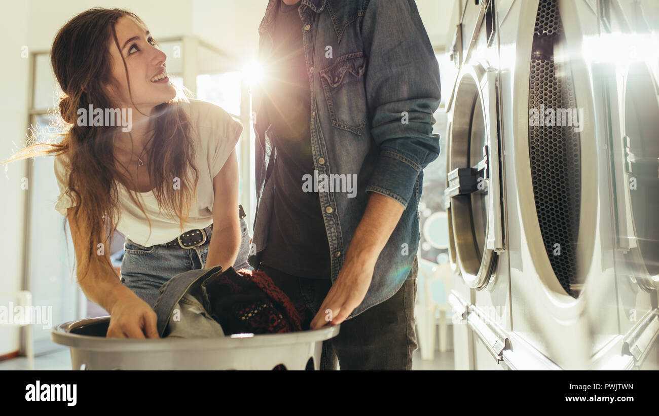 Couple in a laundry room washing clothes with sun flare in the background. Man and woman putting ...