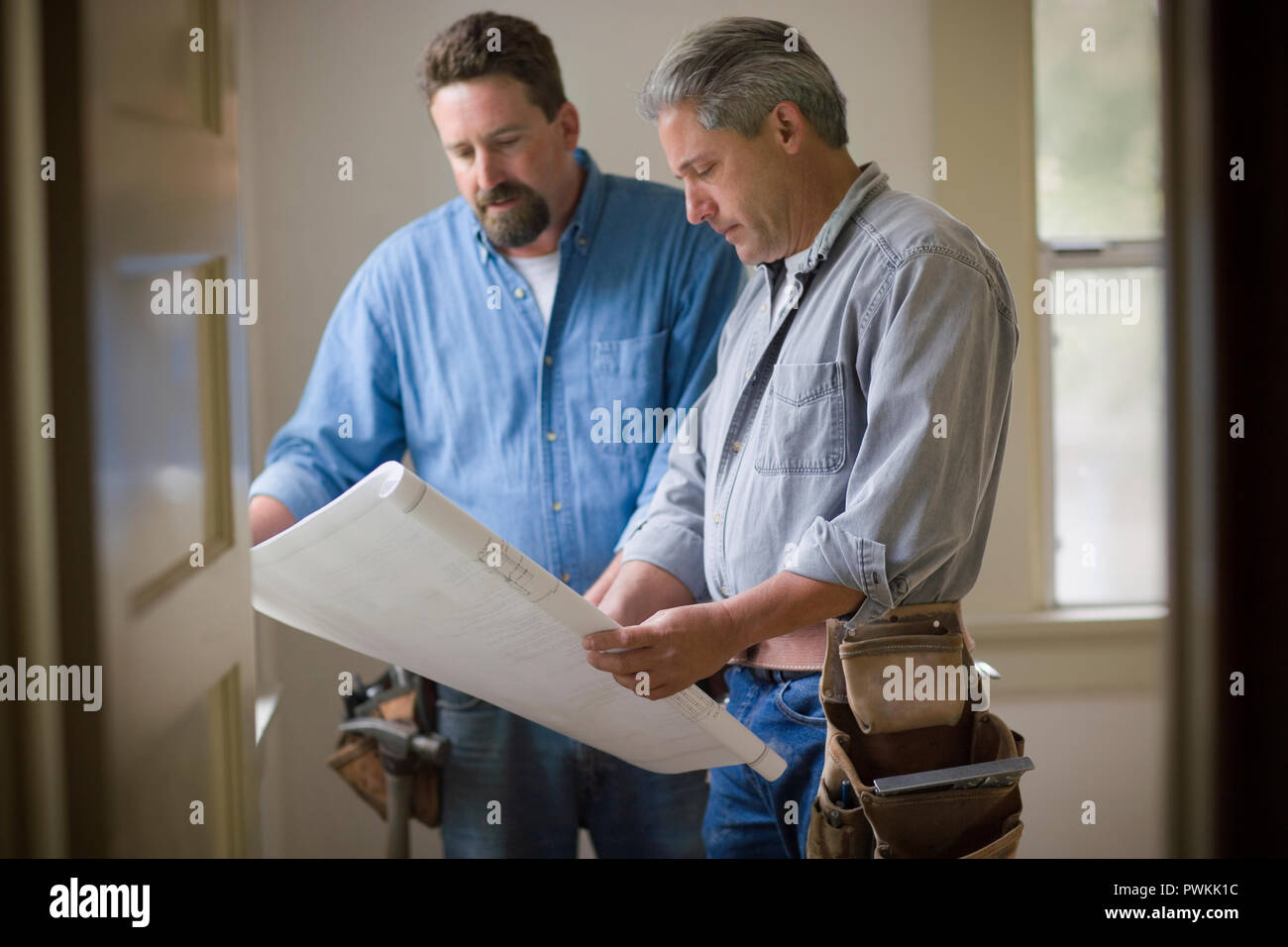 Two male builders looking at a drawing plan inside a house Stock Photo ...