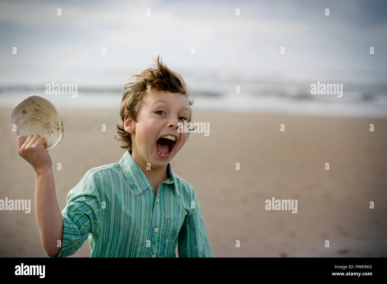 Portrait of a young boy with his mouth open while holding up a large ...
