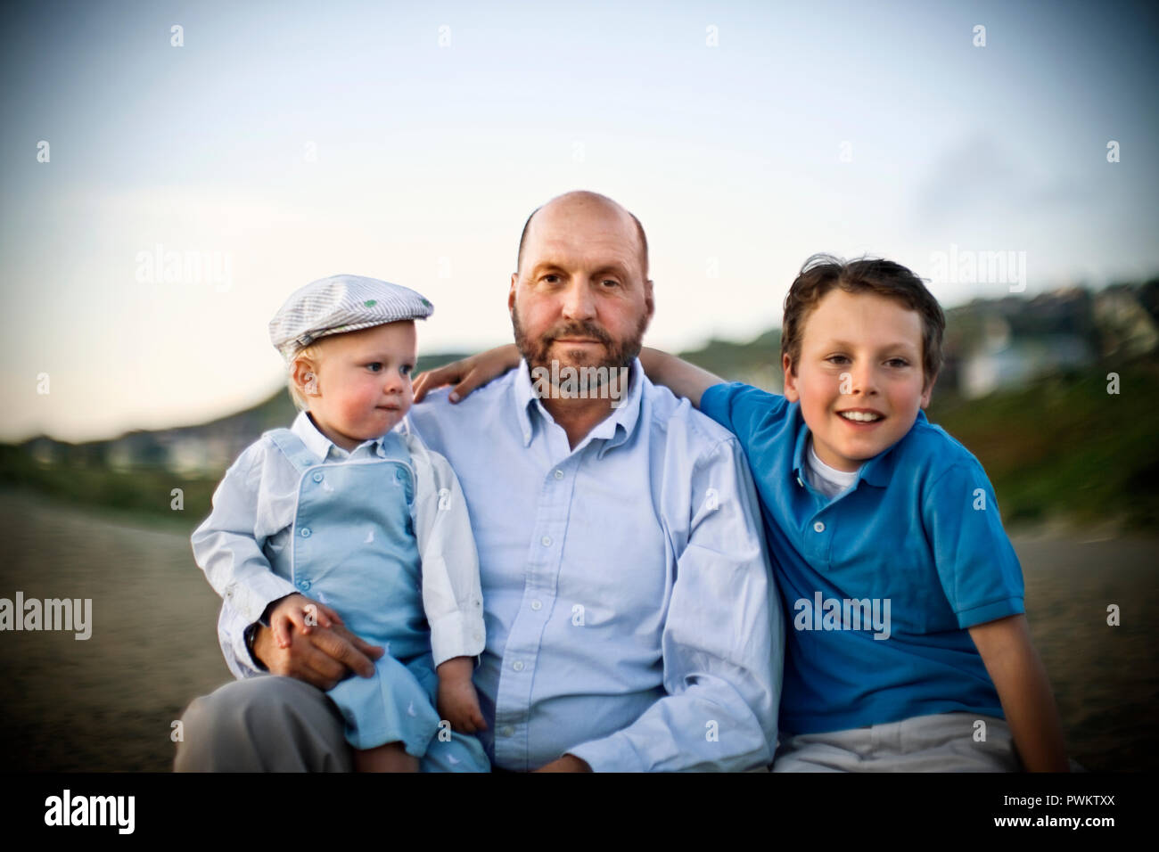Portrait of a mid-adult man sitting with his two young sons on a beach ...