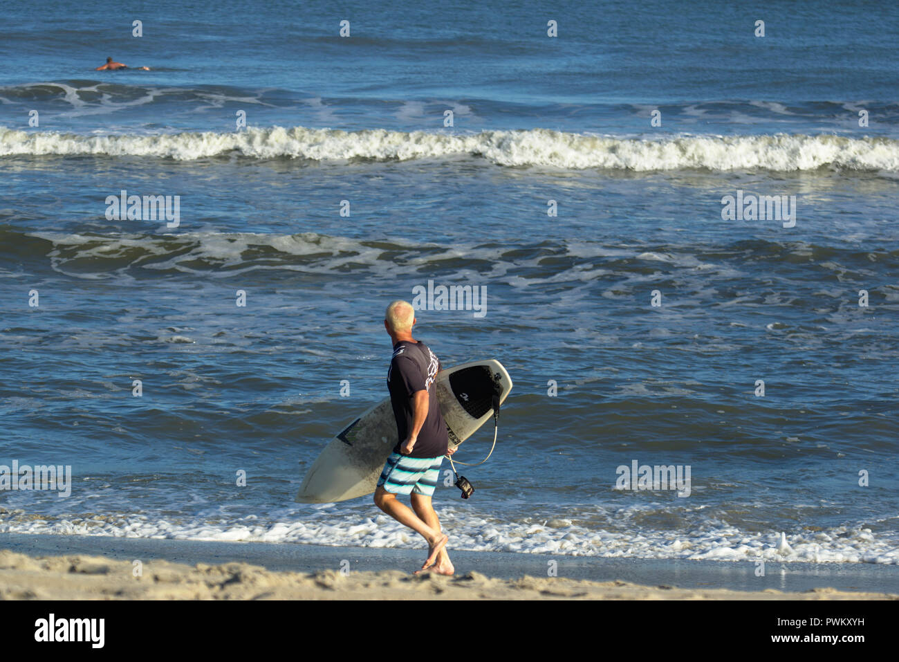 Suffer with board walking along Atlantic Ocean shore Stock Photo - Alamy
