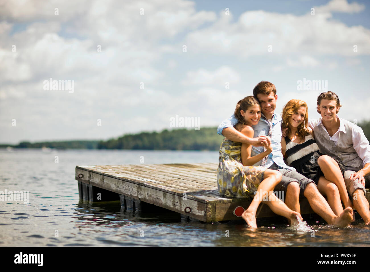 Group of friends sitting on a jetty, splashing in the lake with their ...