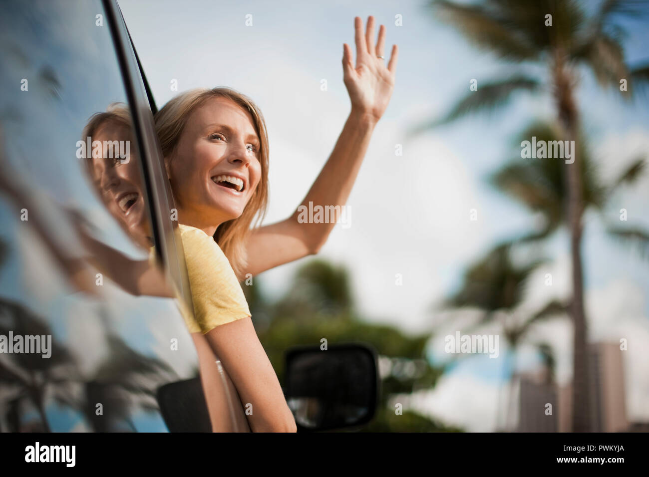 Woman happily waving out of car window Stock Photo - Alamy