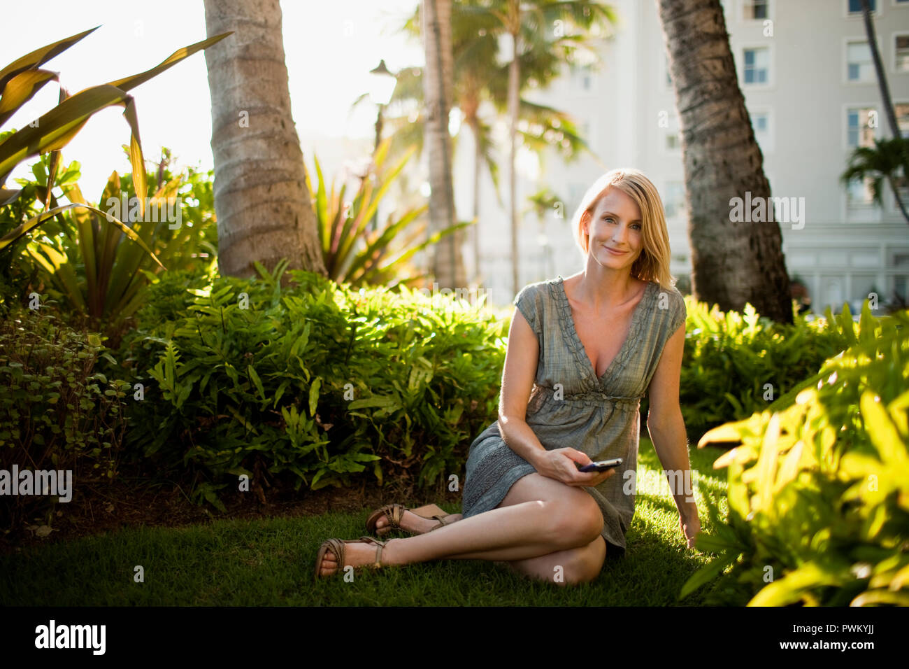 Mid adult woman sitting under palm trees during her summer vacation ...