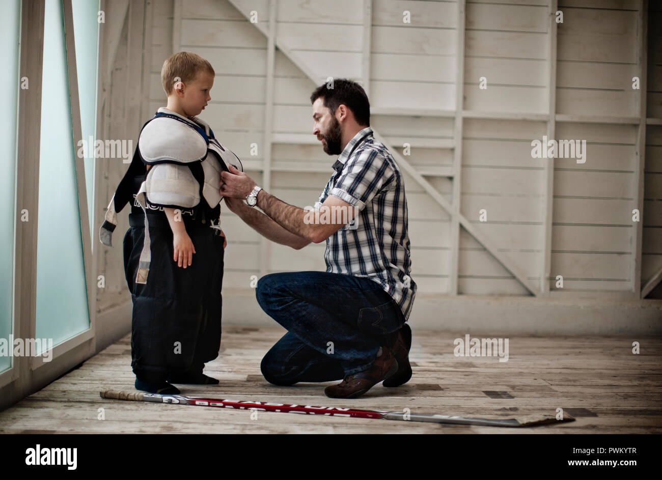Man helping his young son get into his hockey gear Stock Photo - Alamy