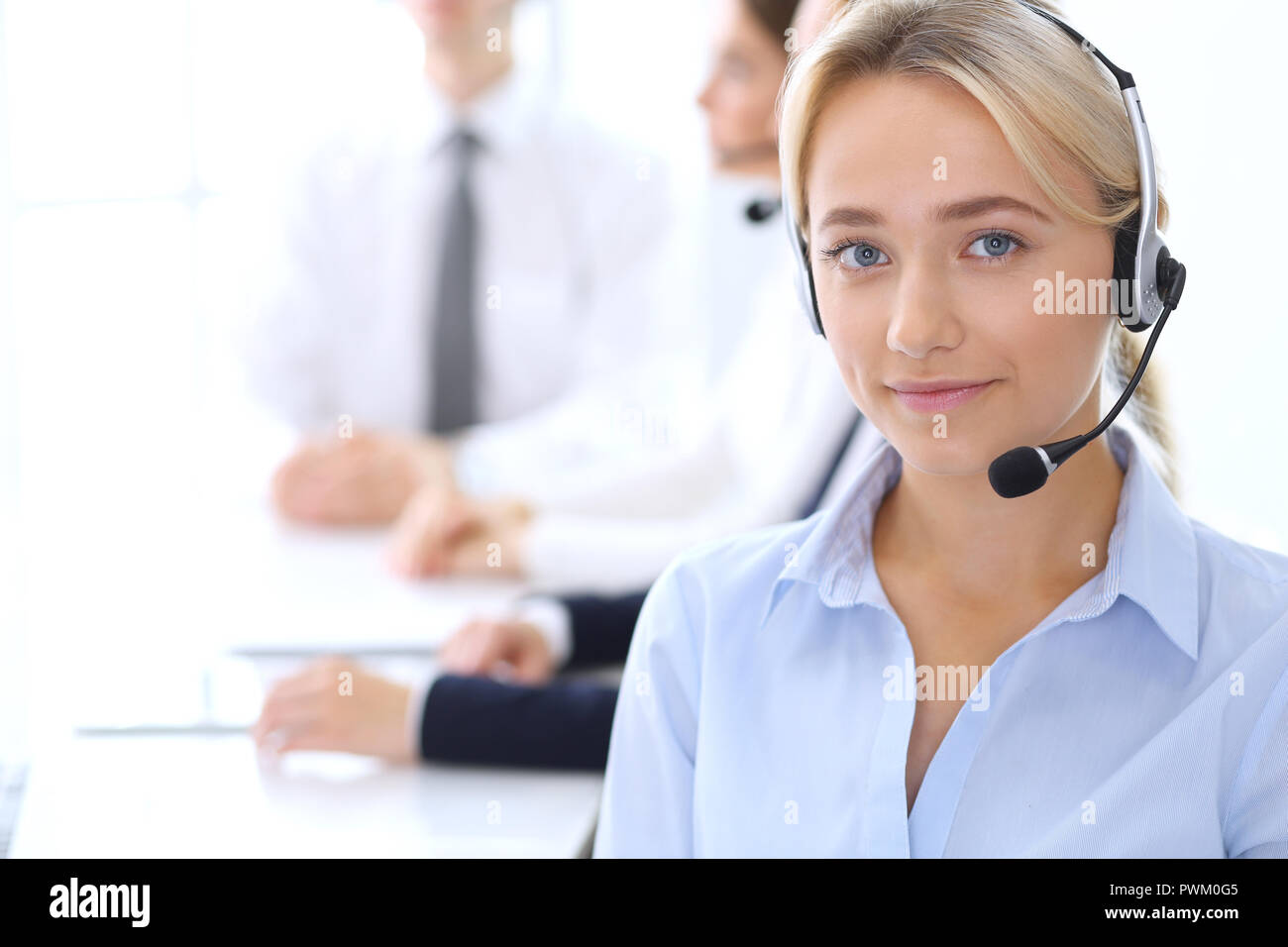 Group of call center operators at work. Focus at blonde beautiful business woman in headset ...