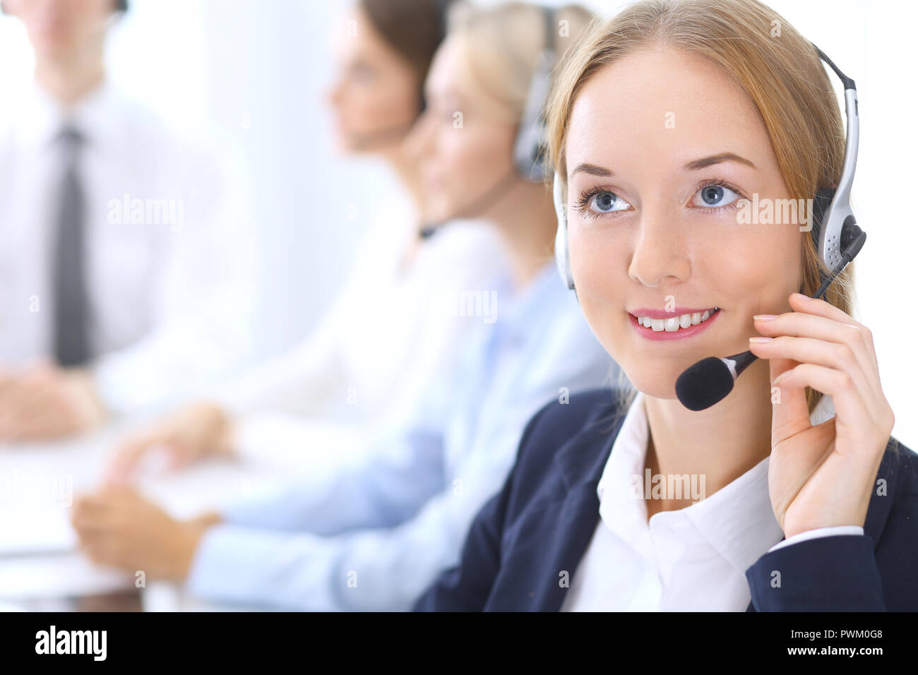 Group of call center operators at work. Focus at blonde beautiful business woman in headset ...