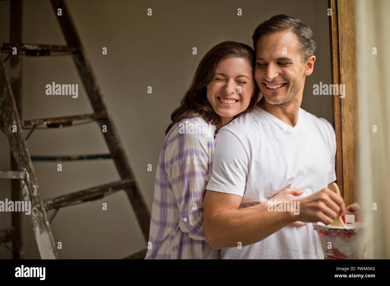 Smiling young wife embraces her handsome husband while they renovate ...
