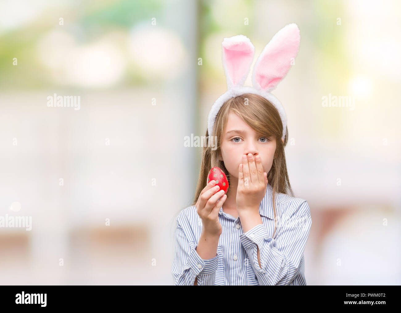 Young blonde child wearing easter bunny ears cover mouth with hand ...
