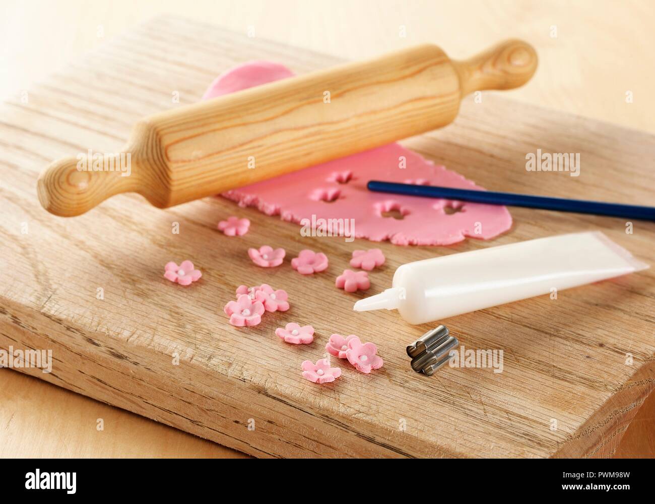 Pink icing rolled out on a board with rolling pin, showing a metal ...