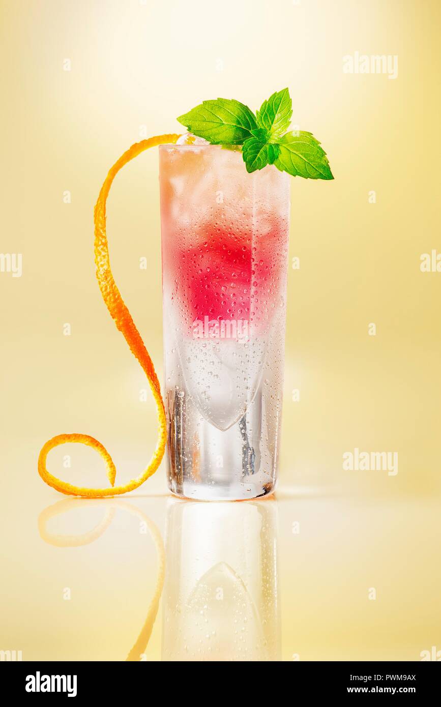 Pink cocktail glass garnished with orange zest on a yellow surface ...