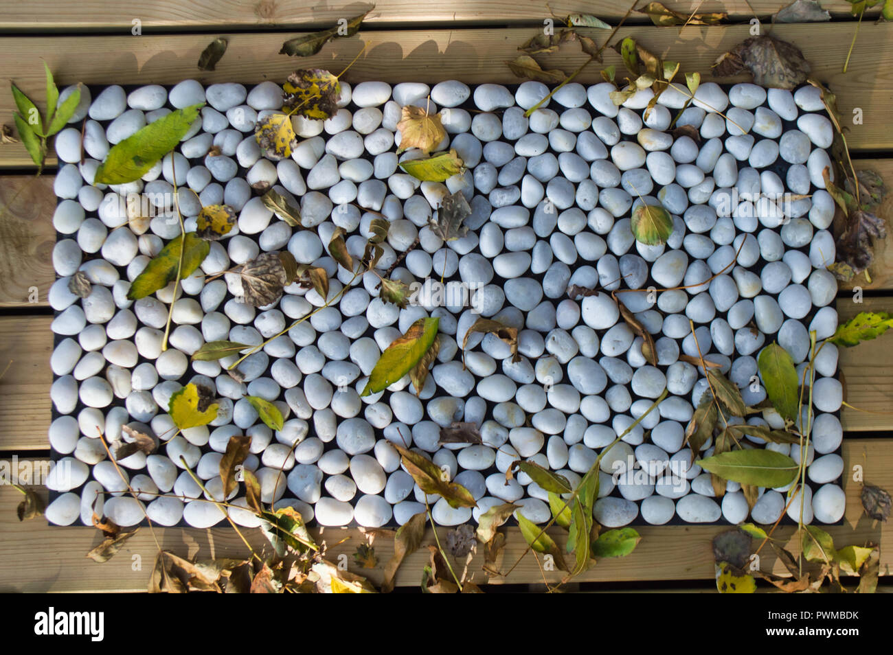 Small stones in pattern on wooden floor with leaves Stock Photo - Alamy