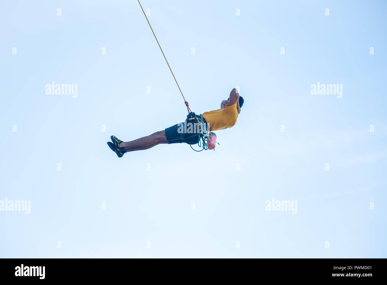View of man without helmet hanging on a rope while rappelling and shows ...