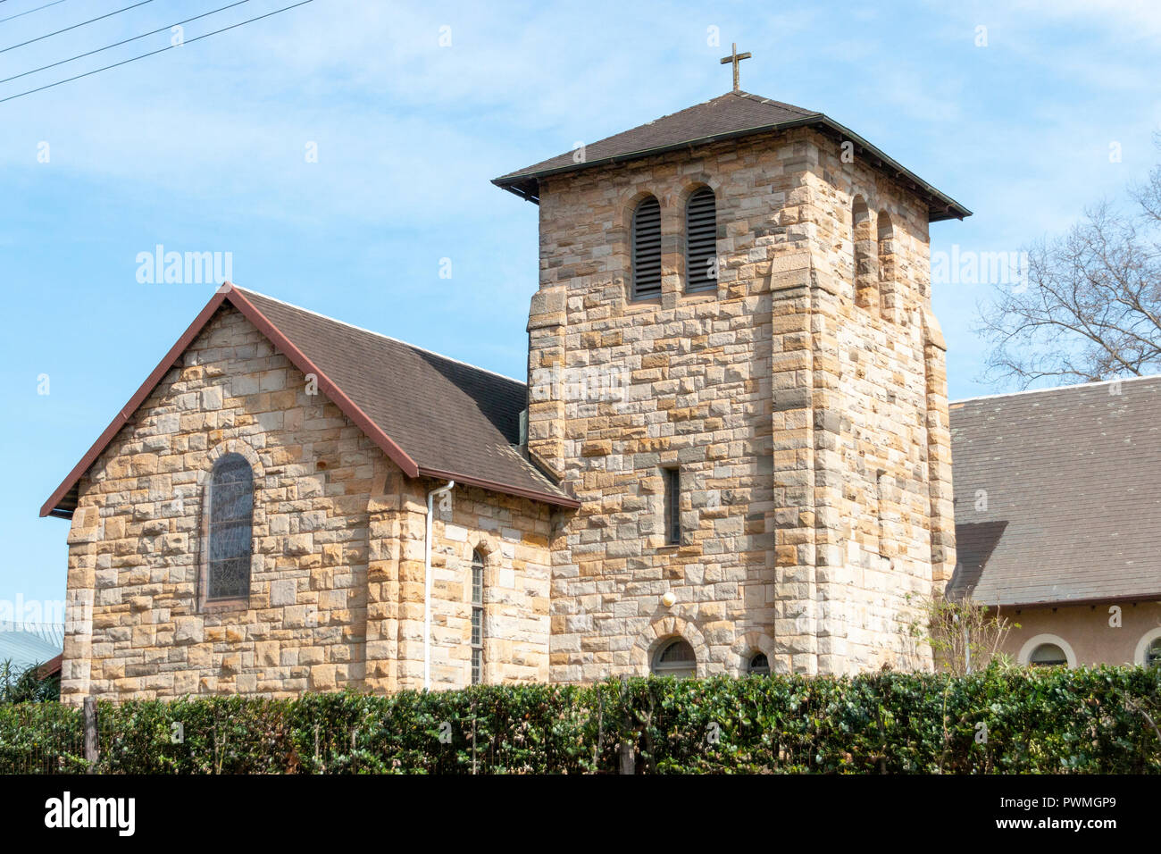 A side view of the top of a stone church with a green plant hedge over ...