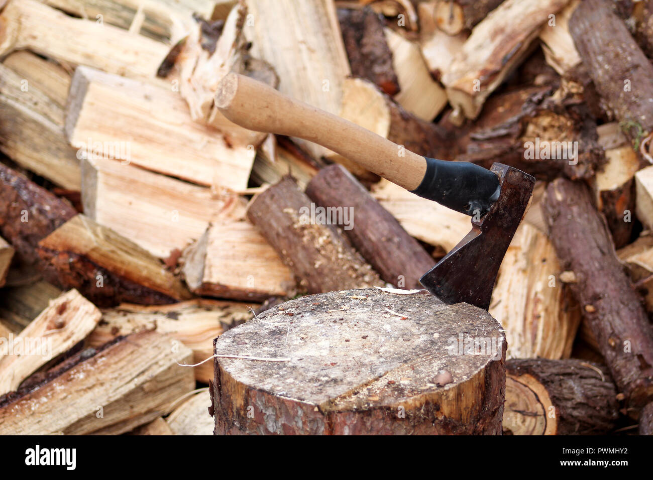 An axe on a wood, tree log. An axe stuck in a log in front of a pile of ...