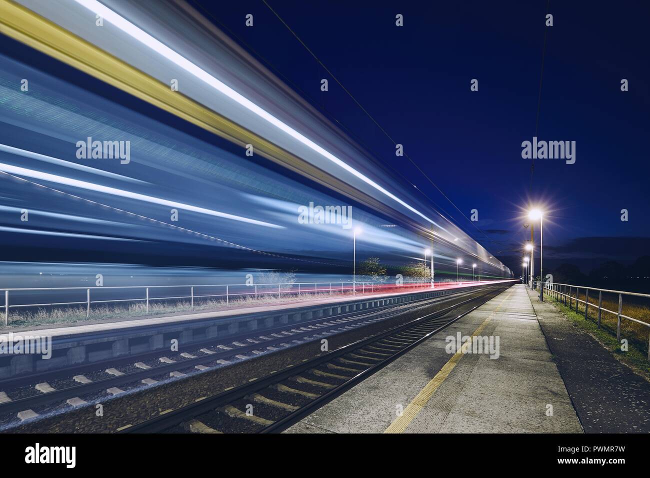 Light trails of passenger train commuting to railroad station at night ...