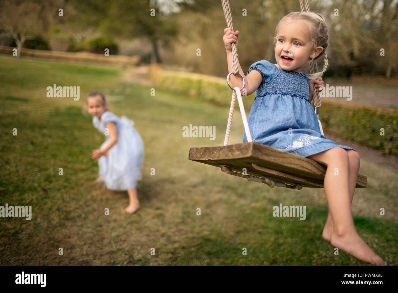 Two happy sisters playing on a swing in the garden Stock Photo - Alamy