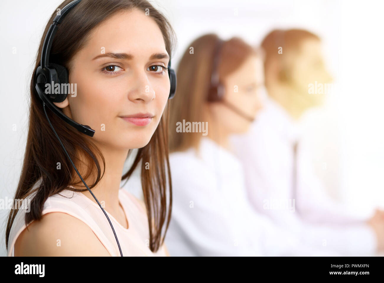 Call center operators. Focus on young cheerful smiling woman in headset. Business and customer ...