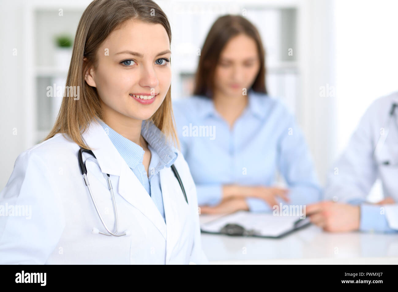 Young beautiful female doctor smiling on the background with patient in hospital. High level and ...