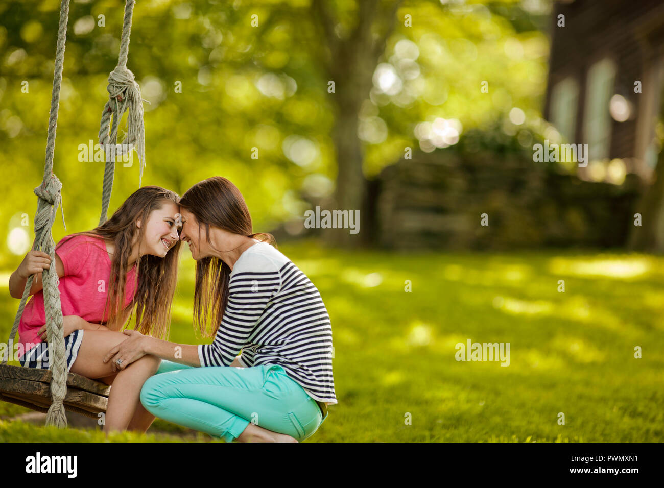Young girl sitting on a rope swing affectionate nudges her mother Stock ...