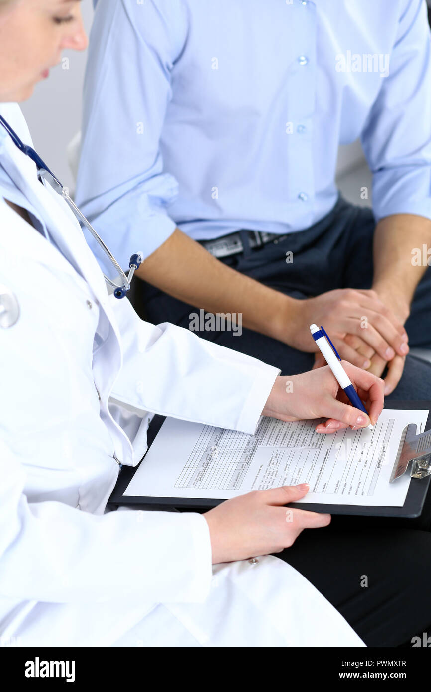 Female doctor holding application form while consulting man patient in ...