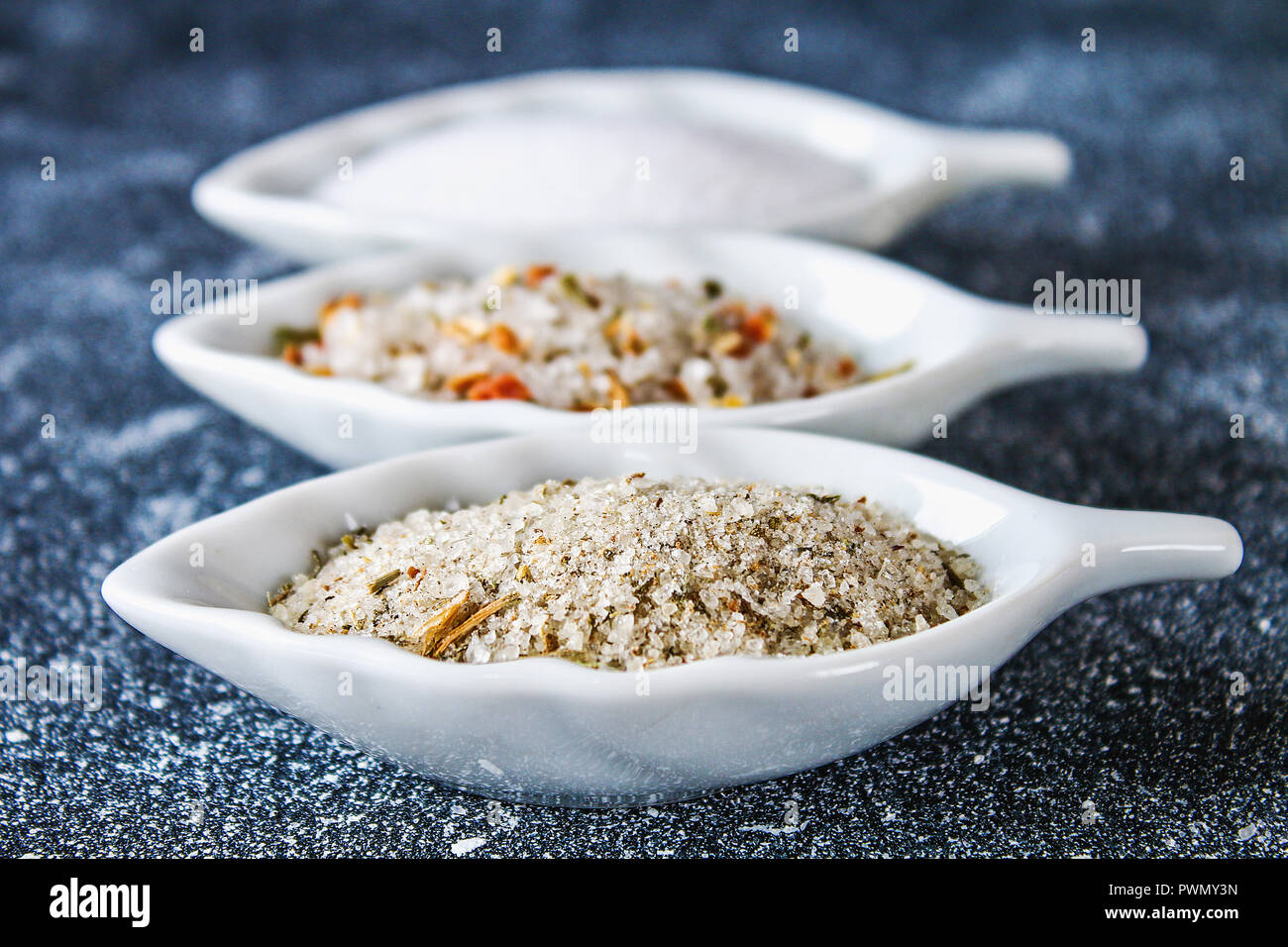 Different types of salt in glass bowls on a dark gray table. Background ...
