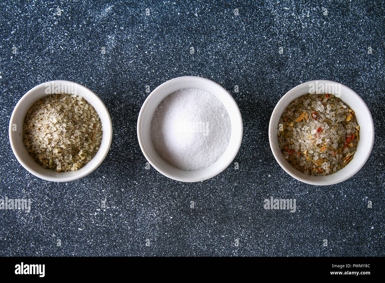 Different types of salt in glass bowls on a dark gray table. Background ...