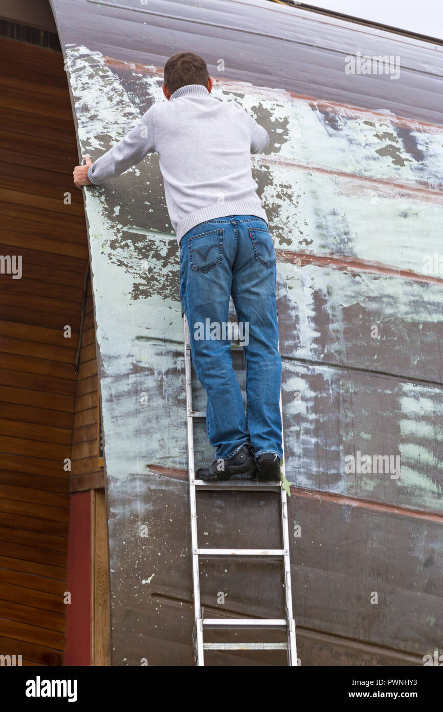 Man up ladder scraping off flaking paint at Weymouth, Dorset in October ...