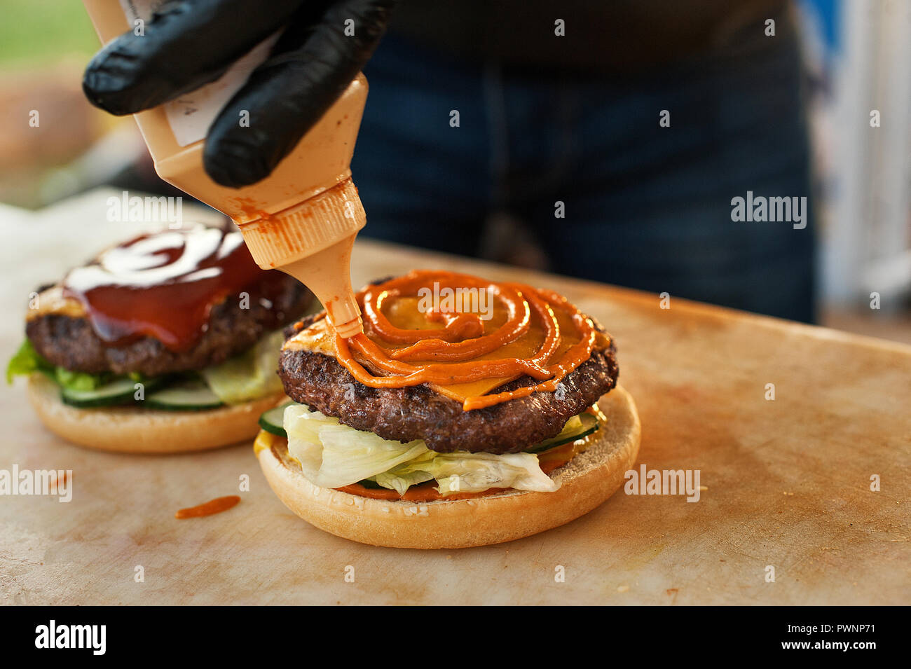The chef prepares a burger in the open air kitchen. Dripping sauce ...