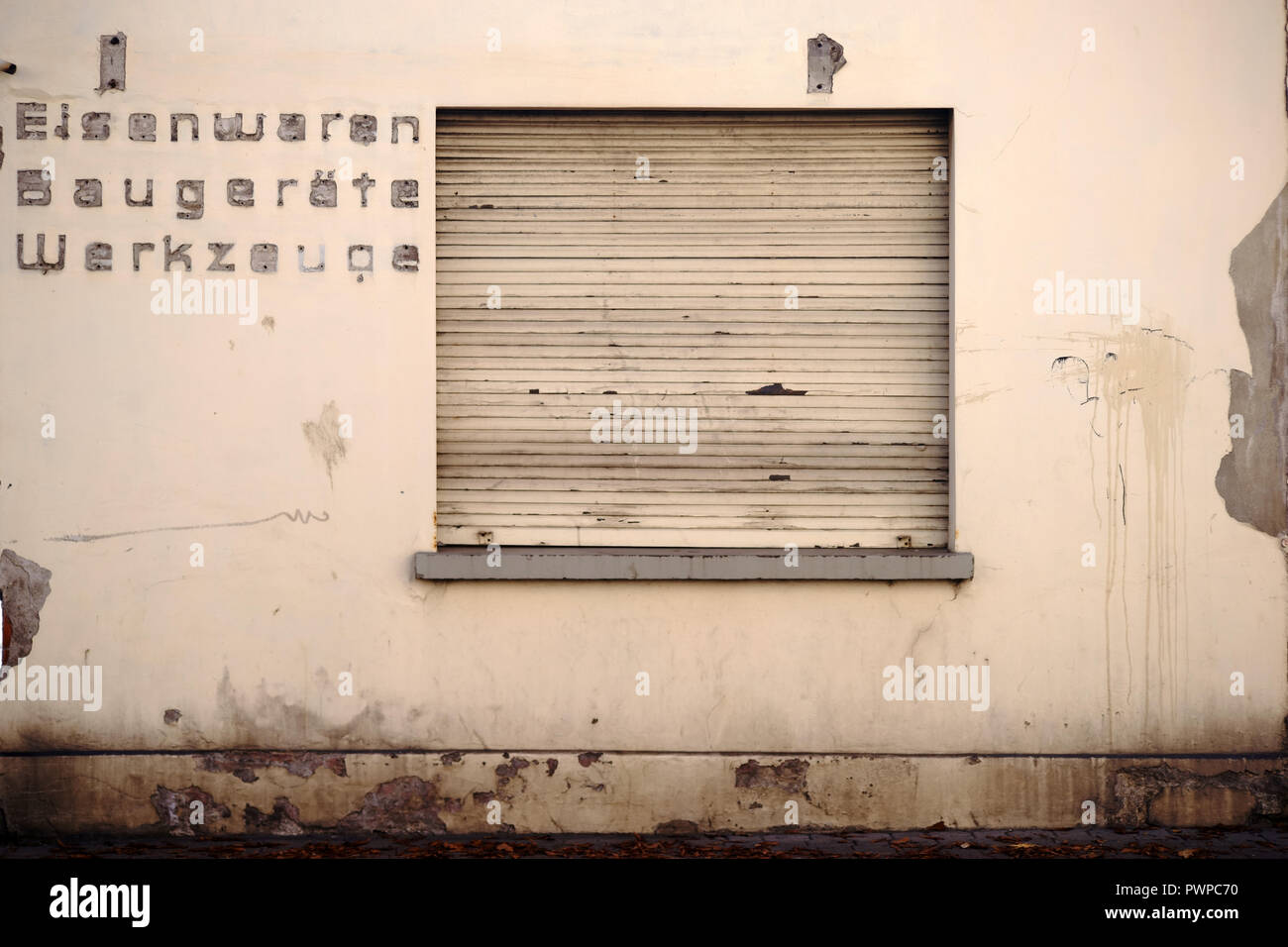 The yellowed facade of a closed hardware store with lowered shutters ...