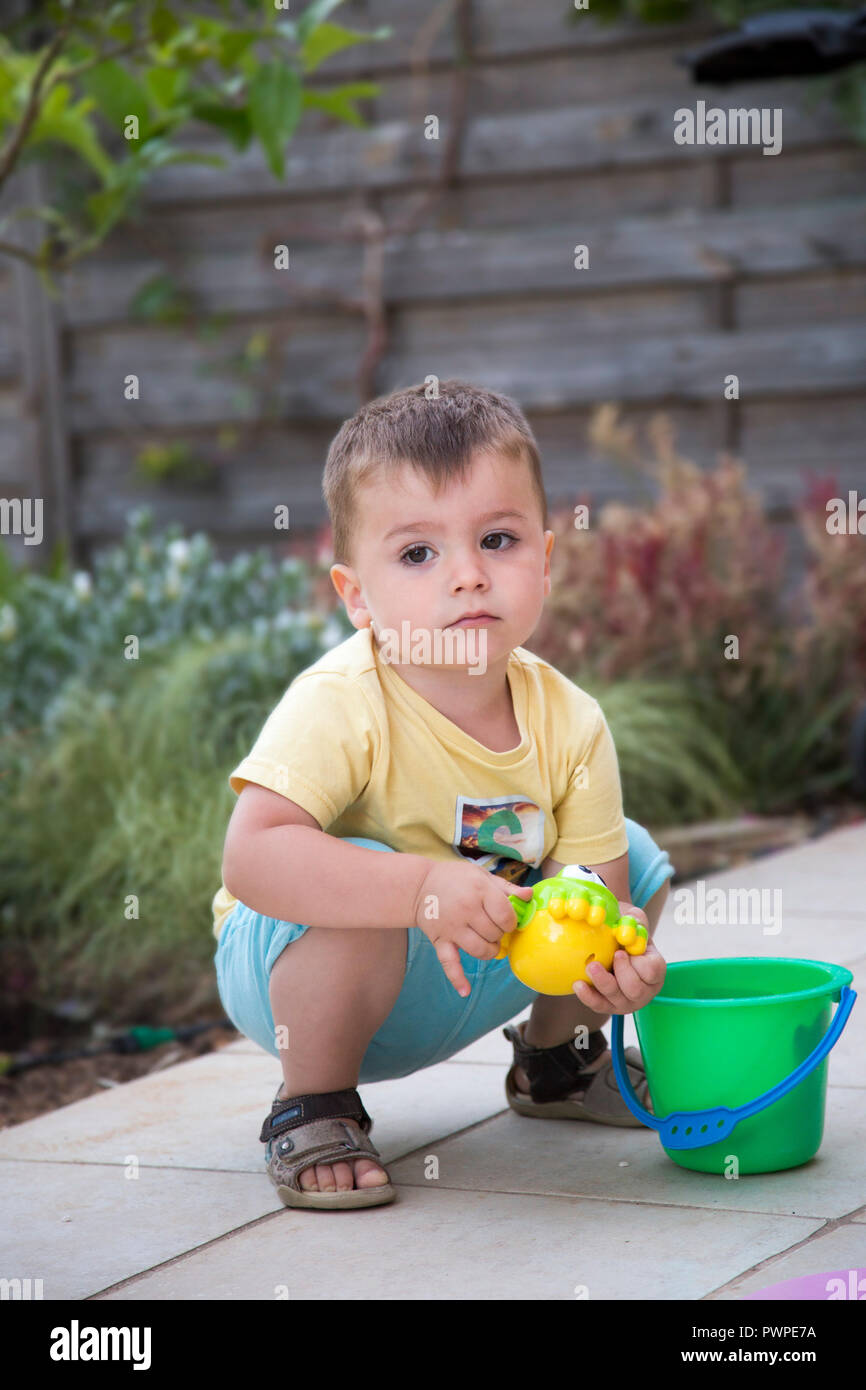 View of a beautiful little sad and pensive boy squatting with her toys ...
