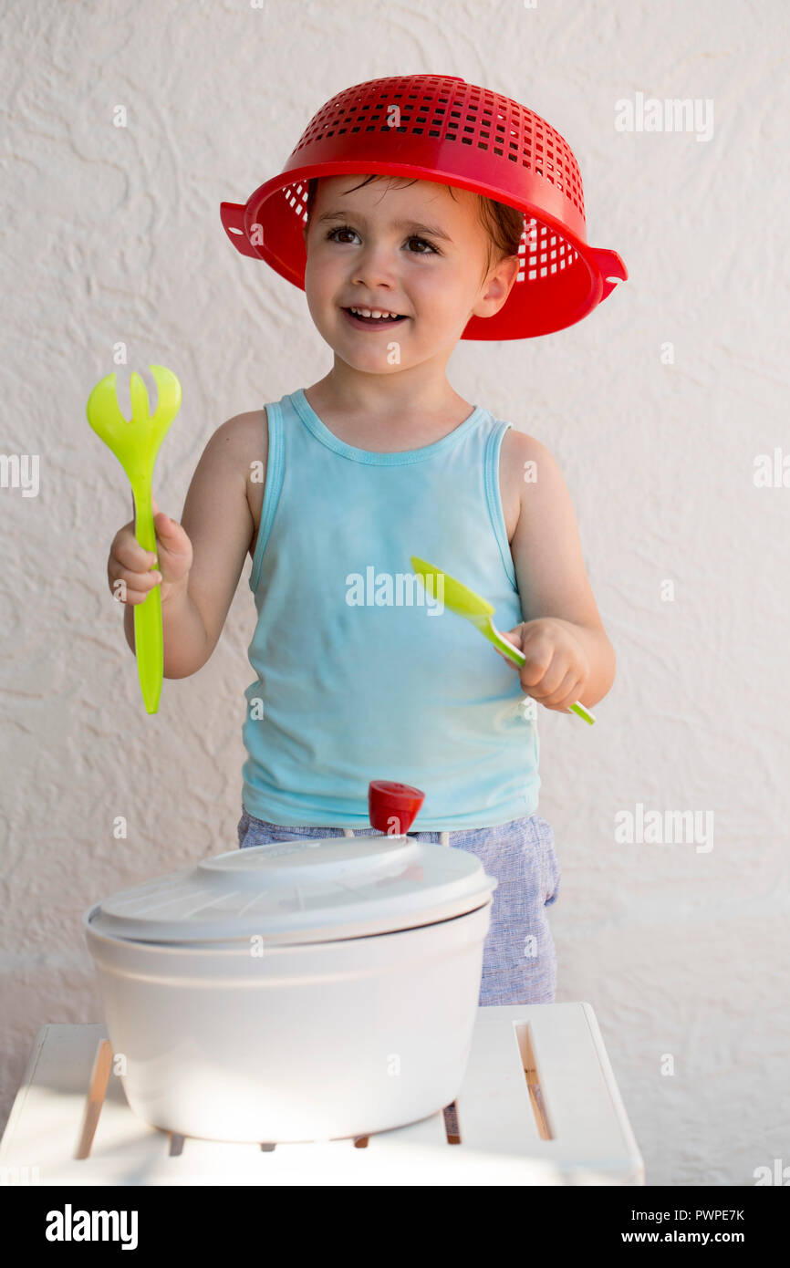 Little boy with a drainer on his head having fun with a wringer and ...