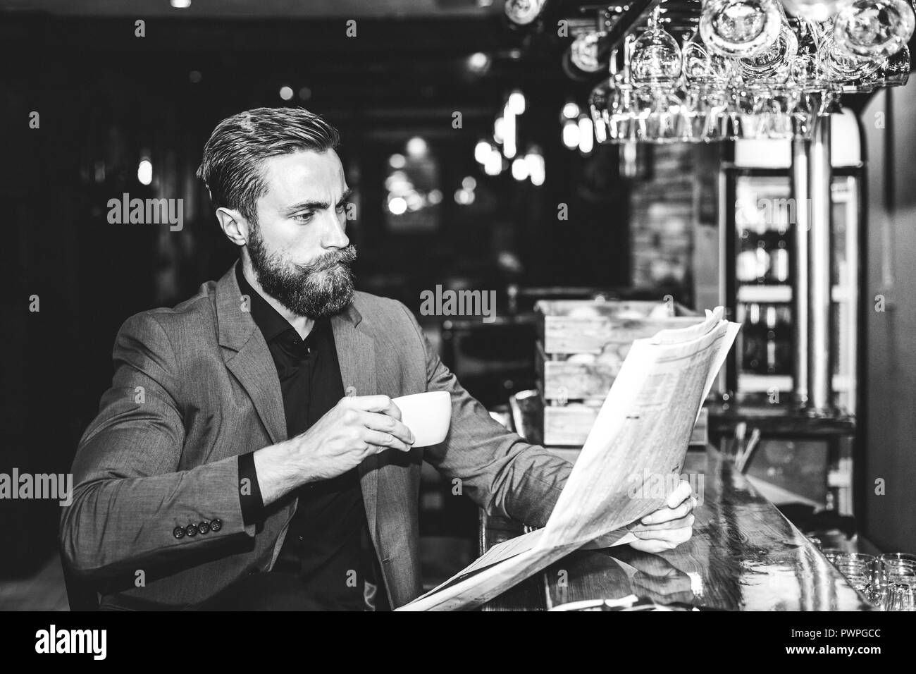 Portrait of a young bearded businessman sitting at the bar, reading ...