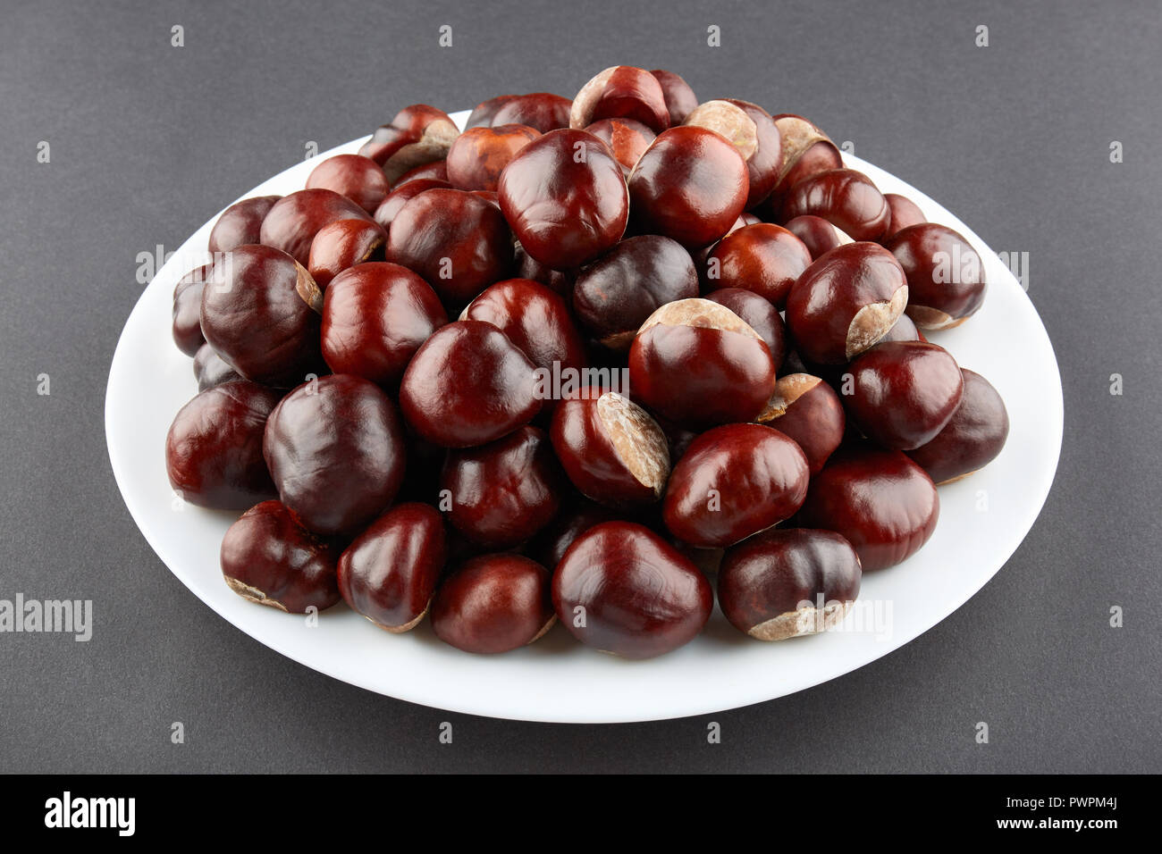 Many chestnuts on white plate. Grey background Stock Photo - Alamy