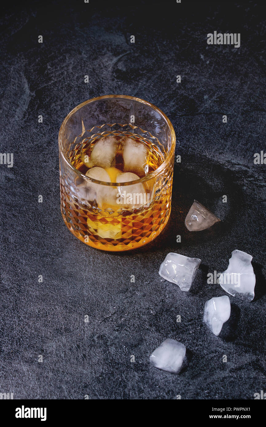 Glass of scotch whiskey on ice standing on black marble table. Alcohol ...