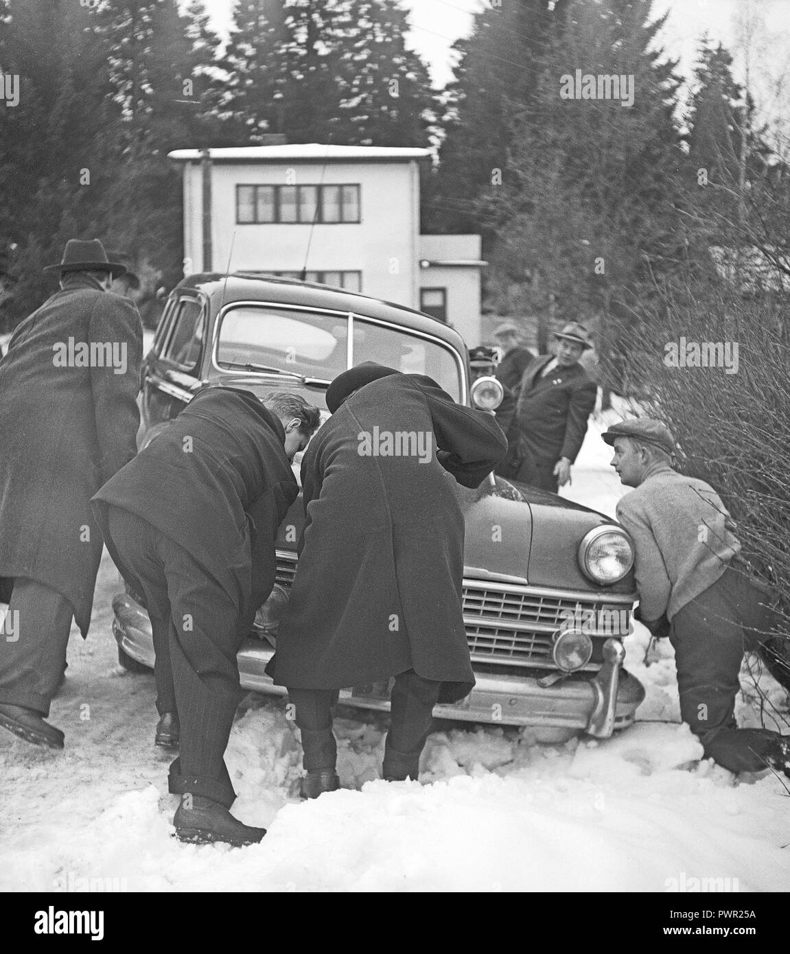 Winter driving in the 1950s. A car has skidded of the snowy road down ...