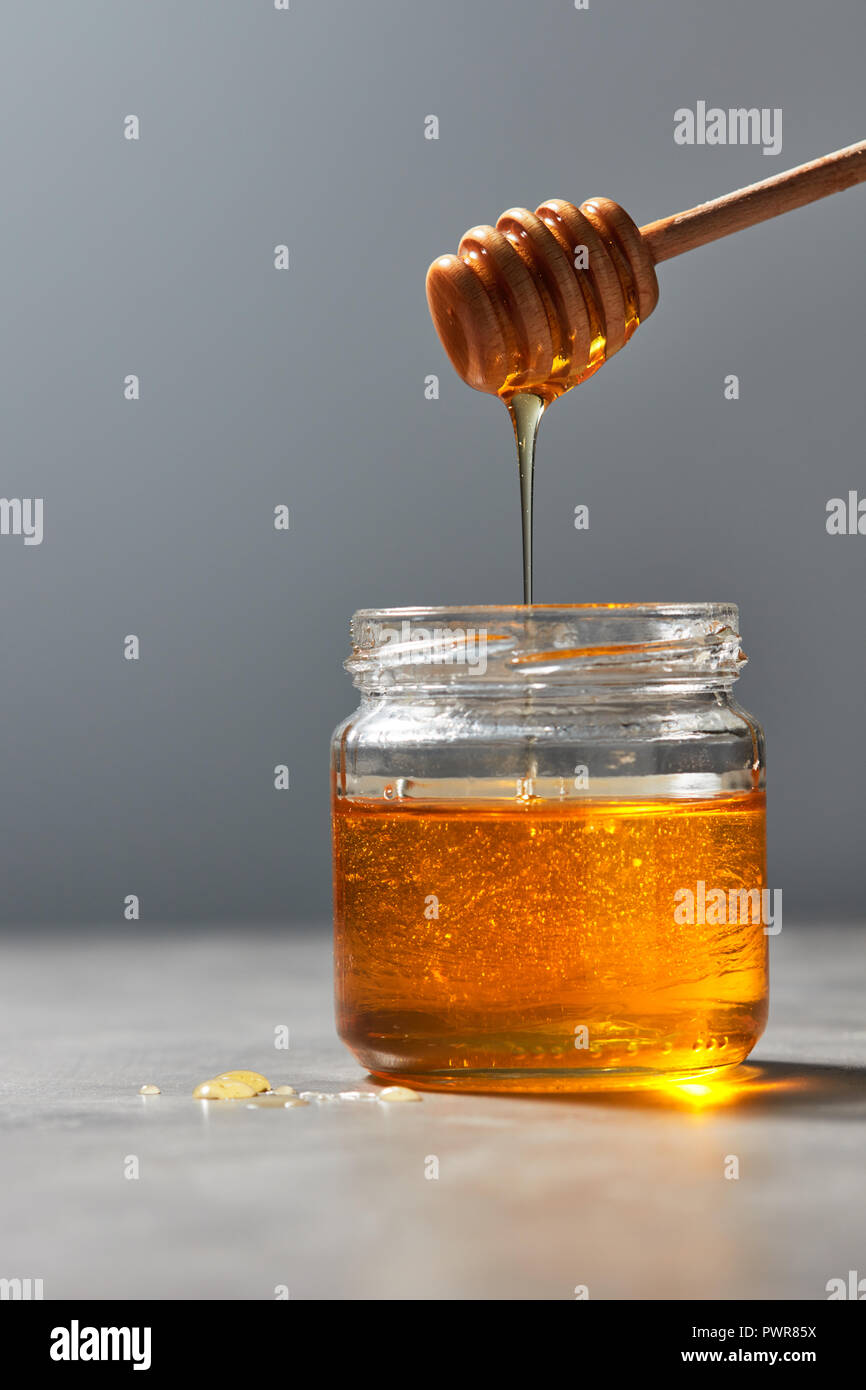 Fragrant natural organic honey drains from wooden dipper into a gray ...