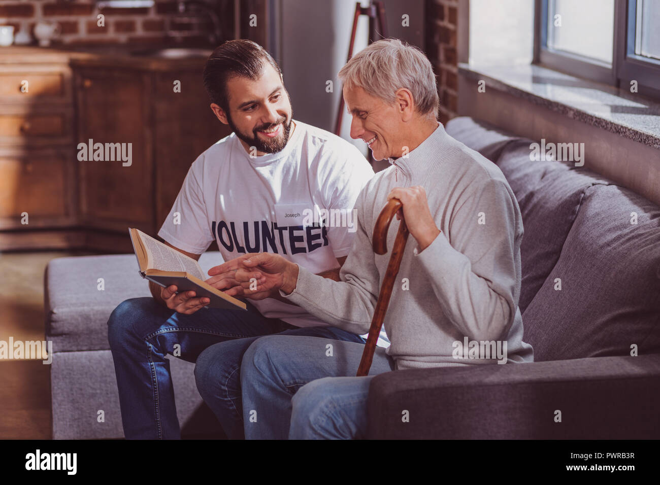 Smiling volunteer reading a book for a pensioner Stock Photo - Alamy