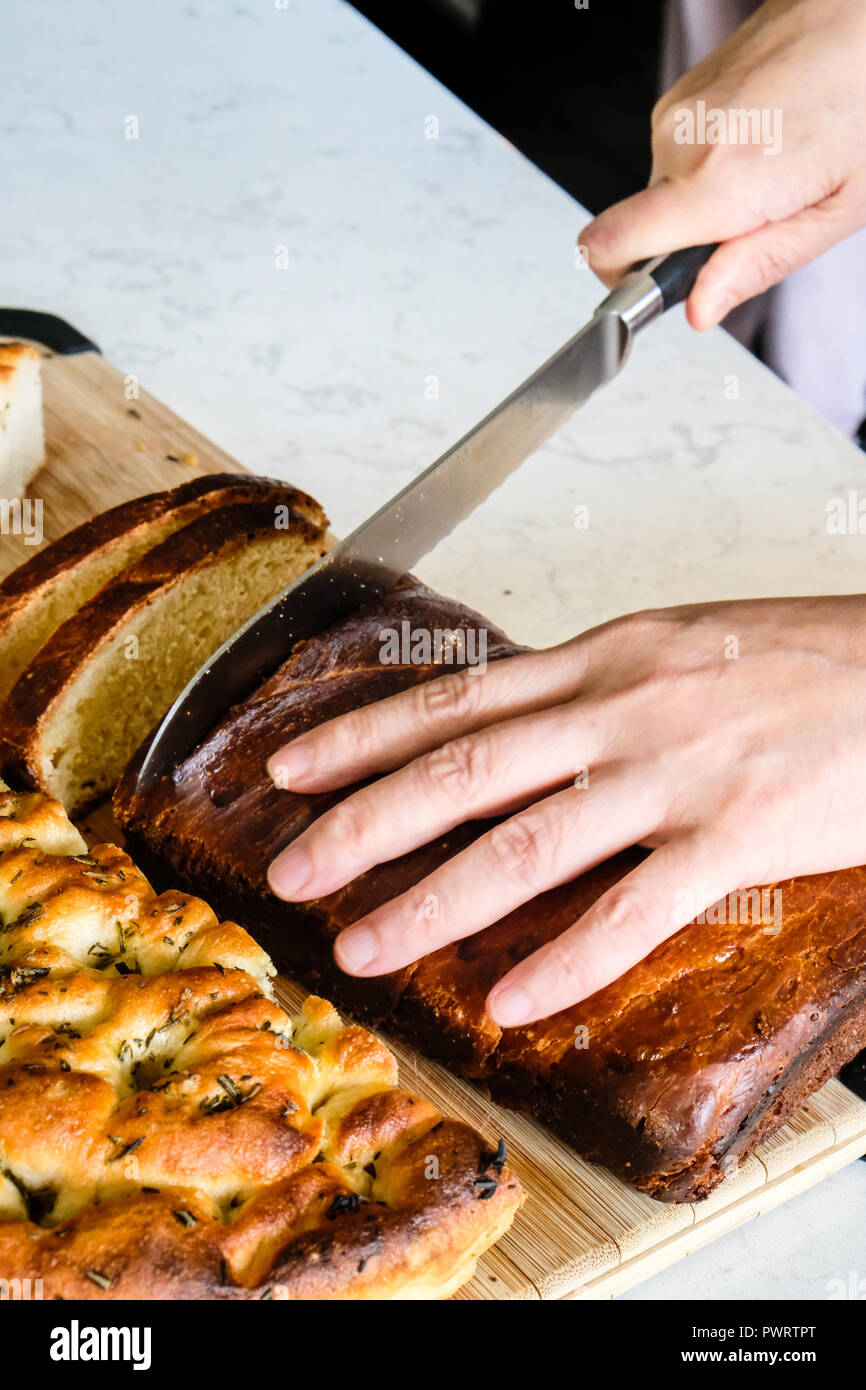 Close up of female hand cutting home made fresh breads on kitchen ...