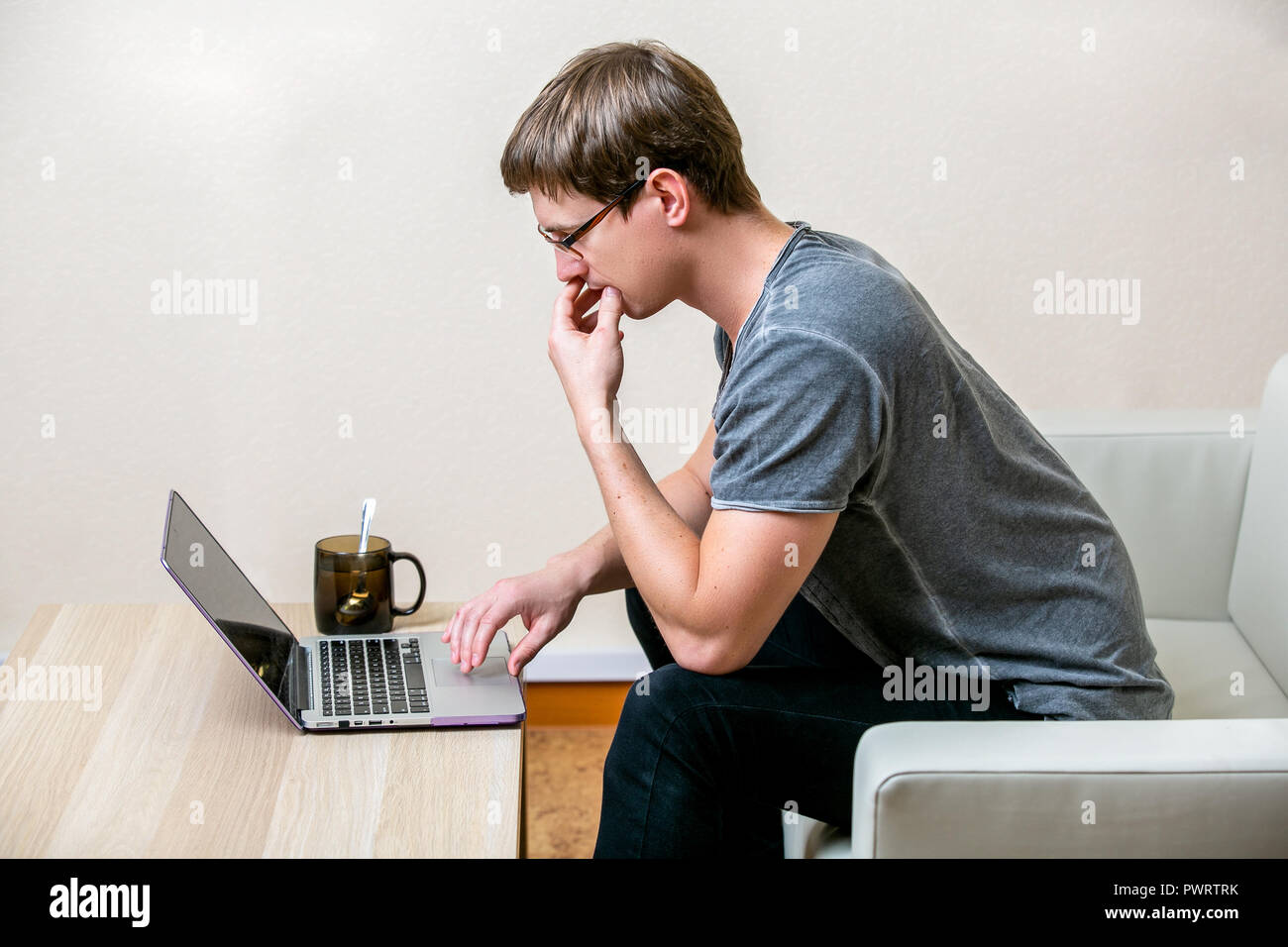 Concentrated young man with glasses working on a laptop in a home ...