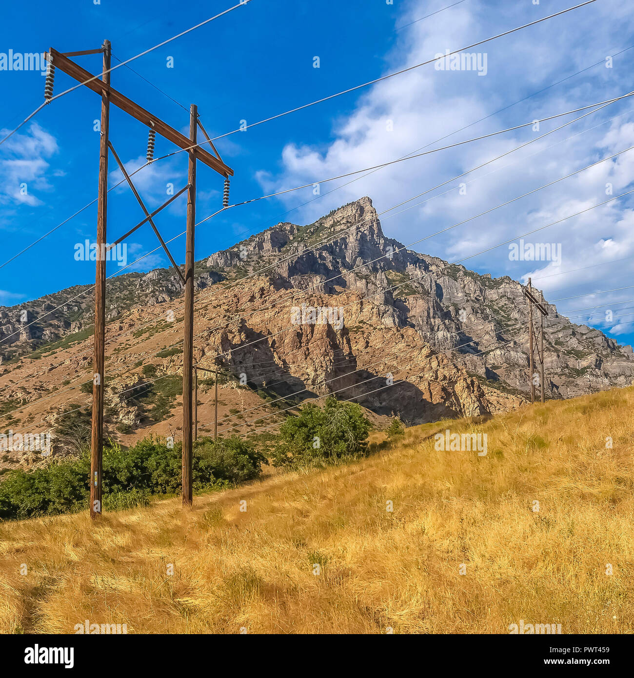 Electricity posts on grass beside a rocky mountain Stock Photo - Alamy