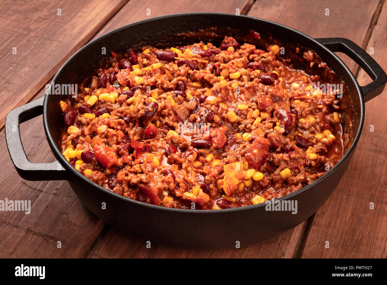 A large cast iron pan with chili con carne on a dark rustic wooden ...