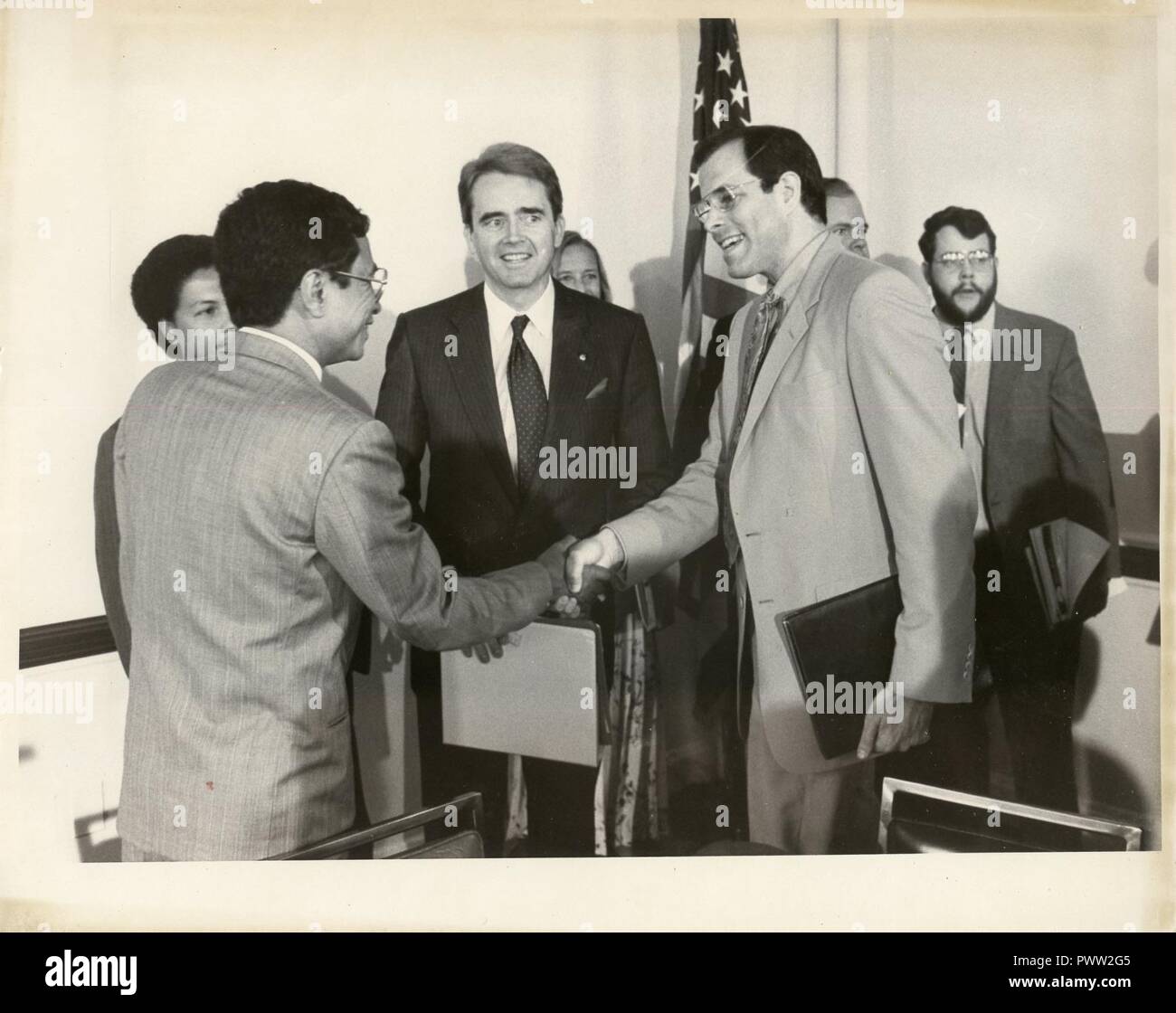 TWO MEN GREETING EACH OTHER WITH OTHER PEOPLE IN THE ROOM Stock Photo ...