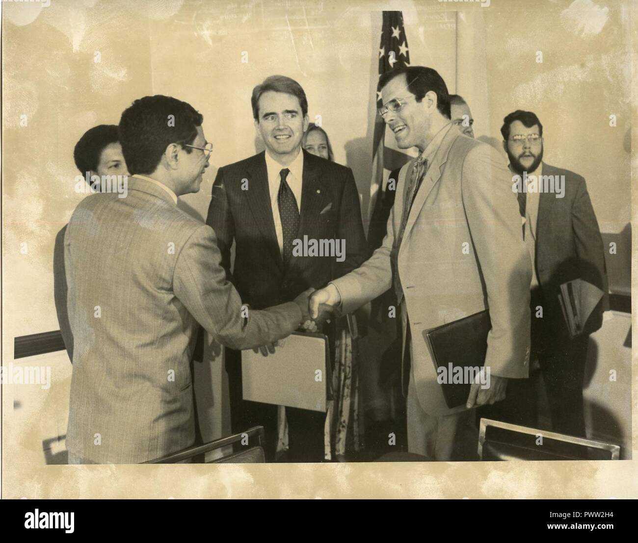 TWO MEN GREETING EACH OTHER WITH OTHER PEOPLE IN THE ROOM Stock Photo ...