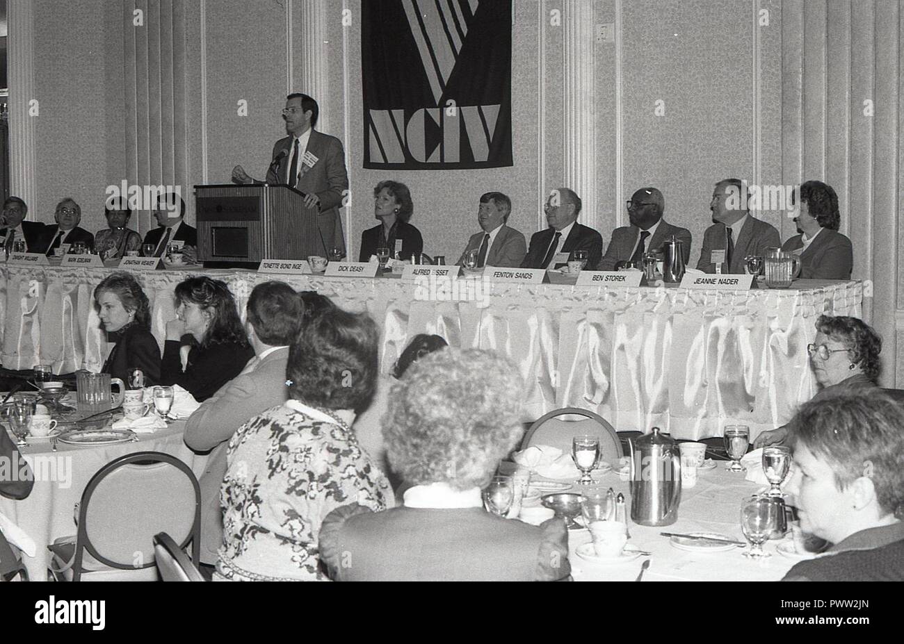 MARK IS AT THE PODIUM GIVING HIS SPEECH TO A GROUP OF MEN AND WOMEN AT ...