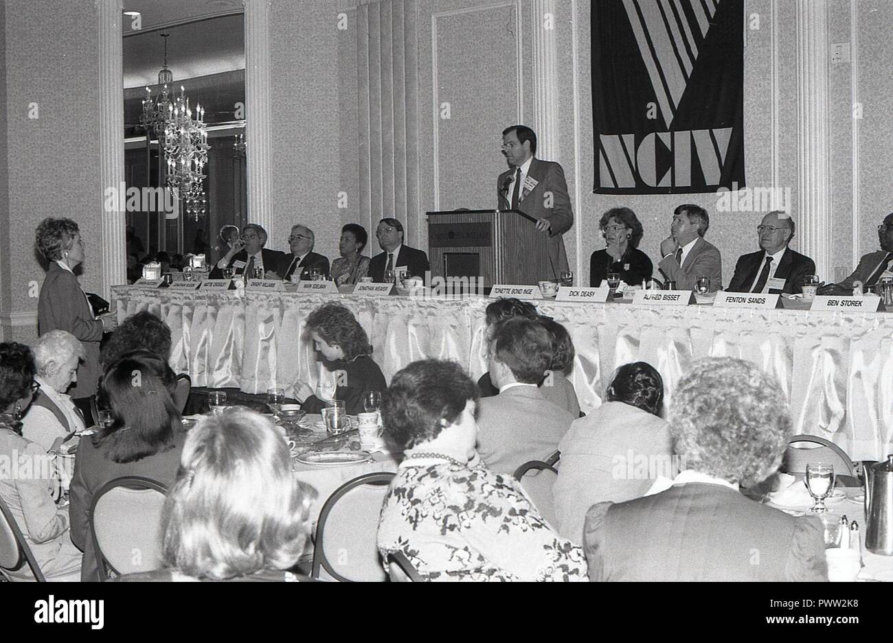 MARK IS AT THE PODIUM GIVING HIS SPEECH TO A GROUP OF MEN AND WOMEN AT ...